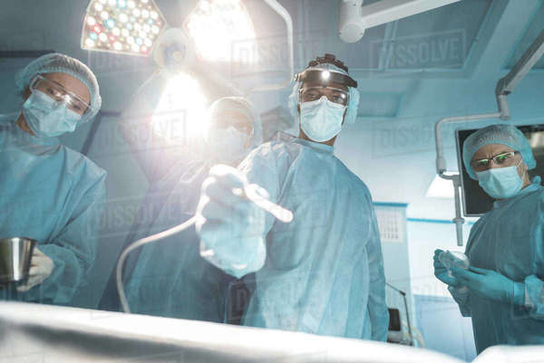 Bottom view of multicultural surgeons looking at camera during surgery ...