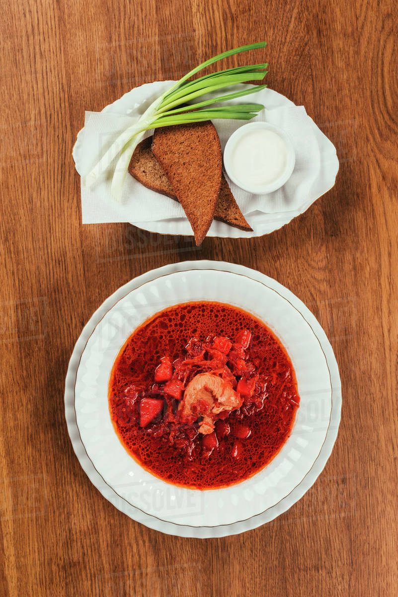 Top view of borscht dish in white plate served with rye bread on wooden ...