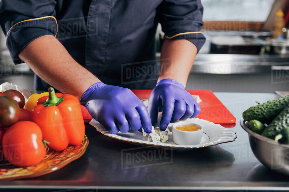 Cropped shot of chef putting cheese slices on plate at kitchen ...