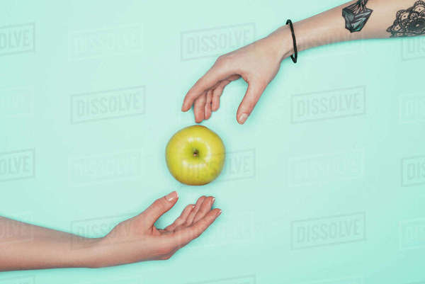 Cropped shot of women passing green apple isolated on turquoise ...