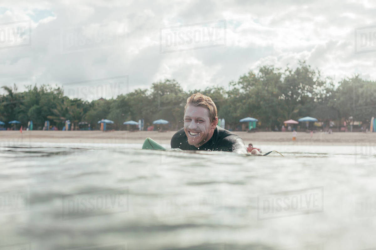 Smiling surfer lying on surf board in ocean, beach on background ...