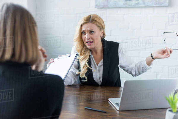 Angry businesswoman gesturing while talking with coworker in office ...