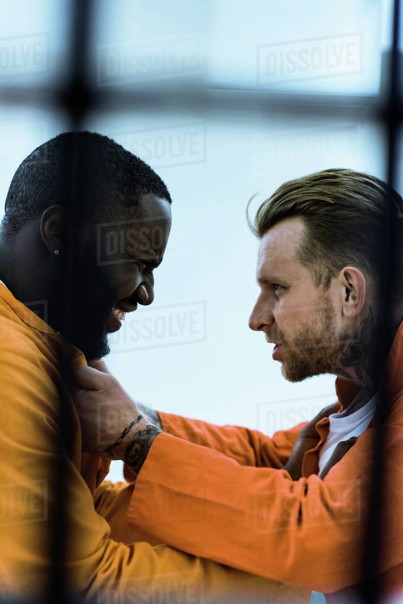 Side view of multiethnic prisoners threatening each other and holding ...