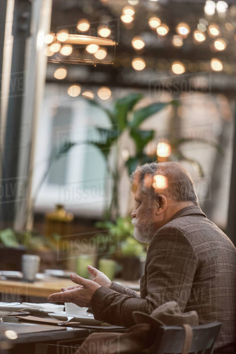 side view of senior man sitting at table with cup of coffee during ...