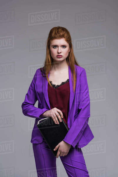 Female fashion model dressed in suit holding handbag isolated on grey ...