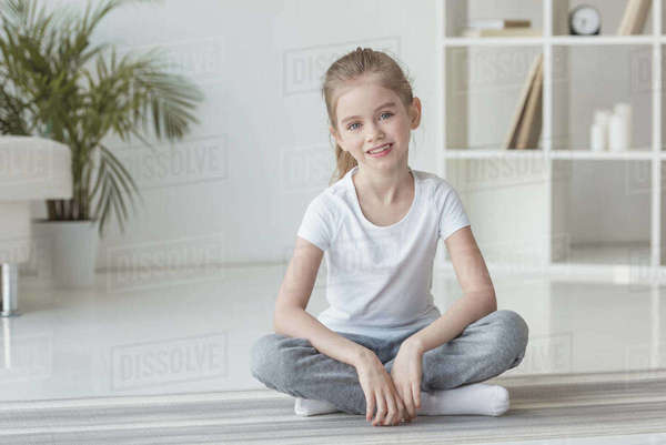 Adorable little child sitting on yoga mat at home - Stock Photo - Dissolve