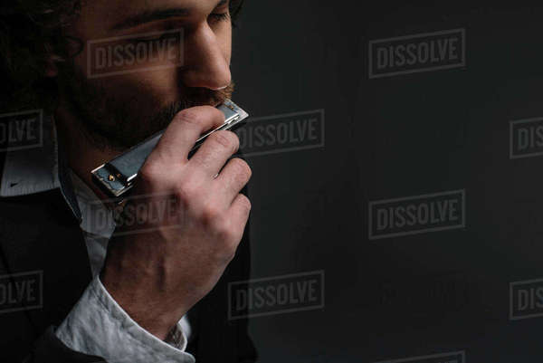 Close-up portrait of handsome musician playing harmonica on black ...