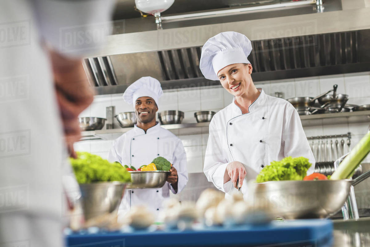 Smiling multicultural chefs preparing food at restaurant kitchen and ...