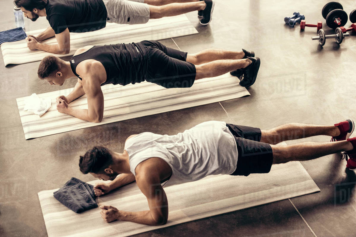High angle view of muscular sportsmen simultaneously doing plank in gym ...