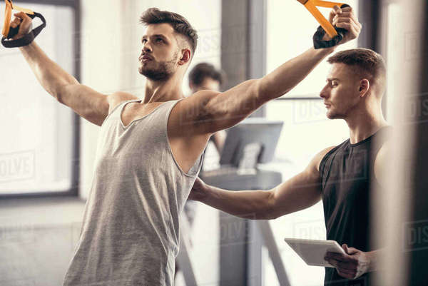 Young trainer with digital tablet looking at sportsman exercising with ...
