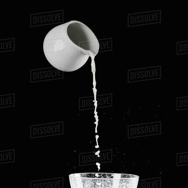 Milk pouring from milk jar into bowl with flour isolated on black ...
