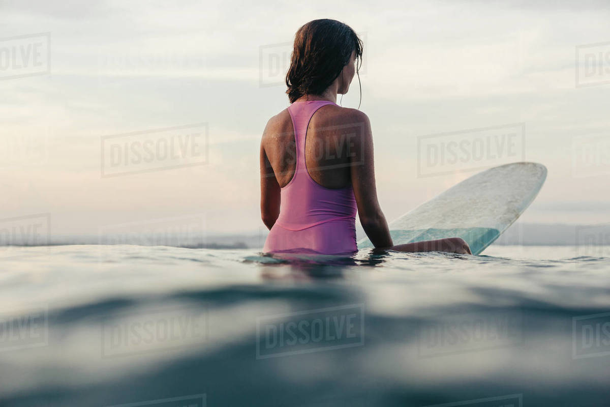 Rear view of sportswoman sitting on surfboard in water in ocean at ...