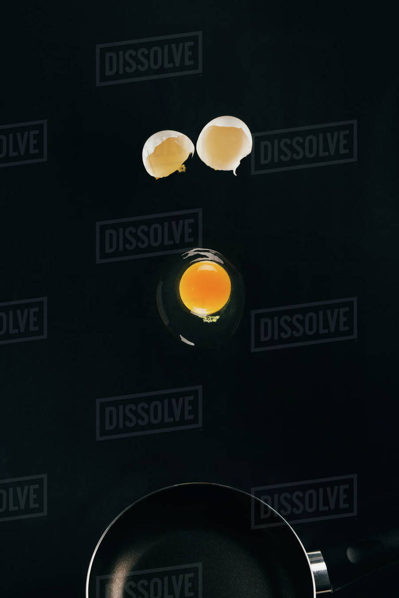 Close up view of raw egg yolk falling on frying pan isolated on black ...