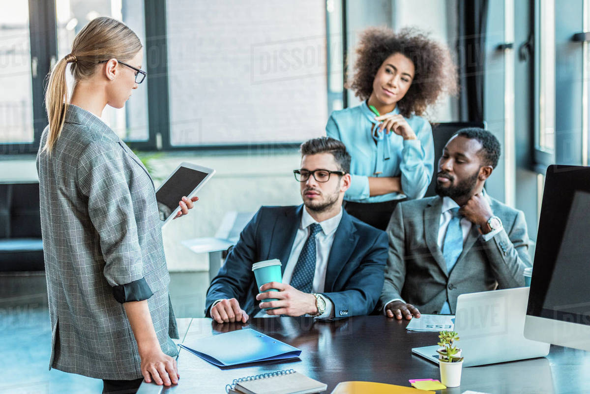 Multicultural businesspeople looking at businesswoman with tablet in office - Stock Photo - Dissolve