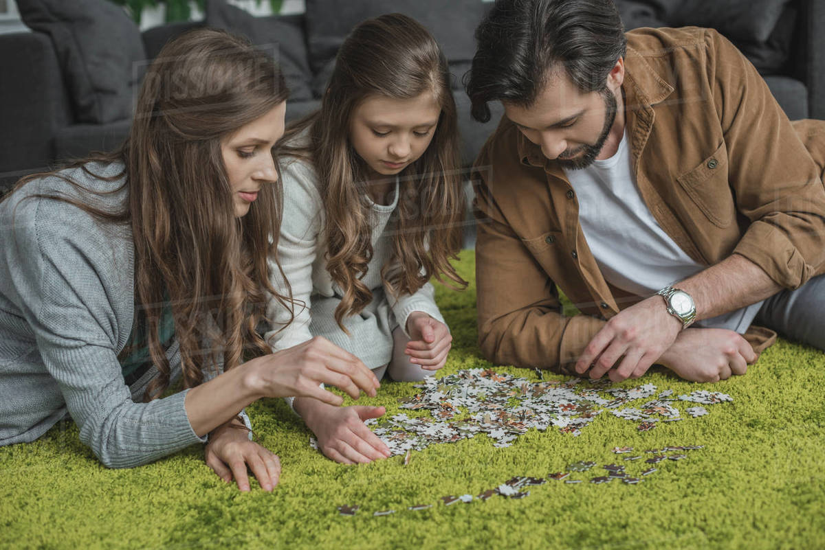 Parents and daughter connecting puzzle pieces on floor in living room ...