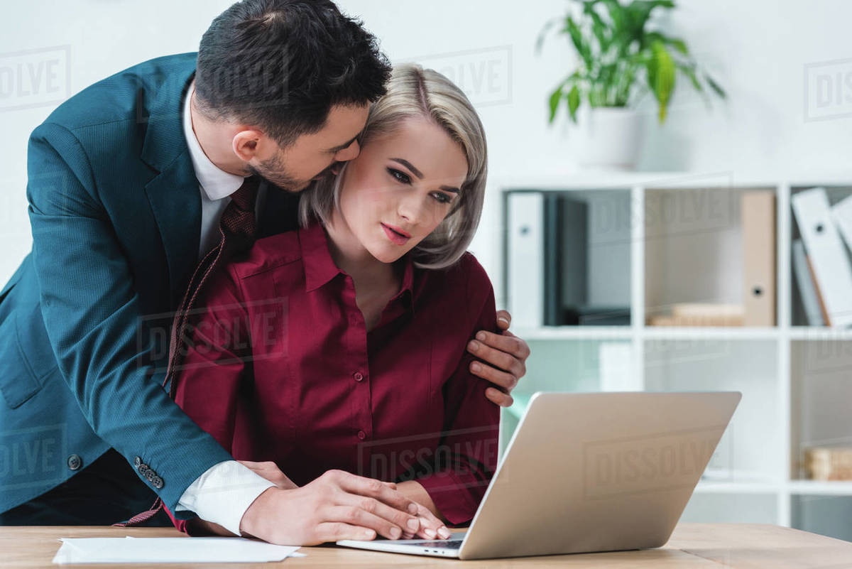 businessman flirting with beautiful female colleague using laptop in ...