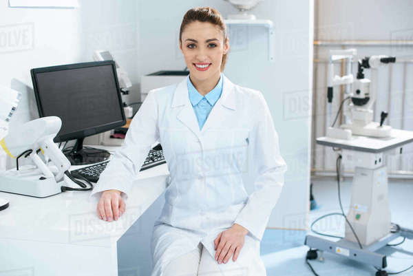 Beautiful female optician working in clinic with computer on background ...