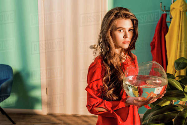 Stylish woman in red dress holding aquarium with gold fish and looking ...