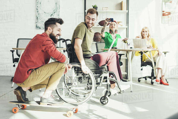 Disabled businessman with laptop with colleague on skateboard and ...