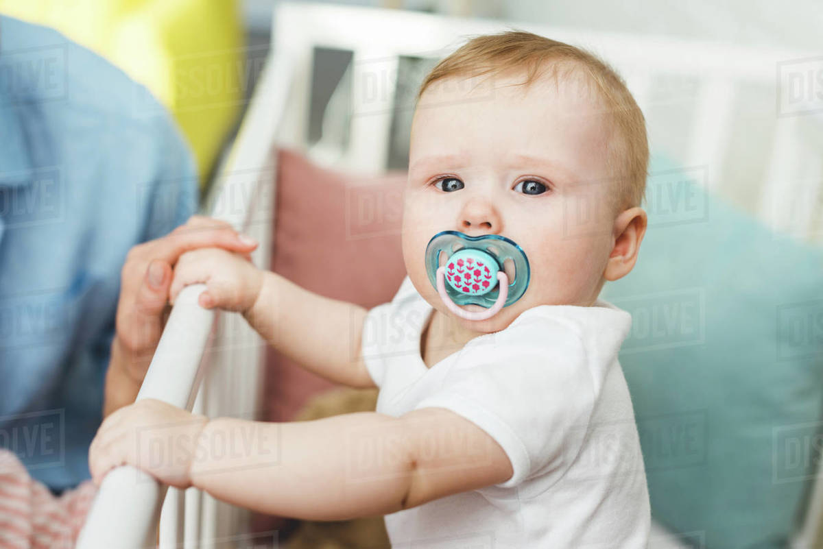 Cropped view of parents and infant daughter with baby dummy in crib ...