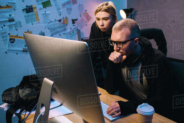 Serious couple of hackers working with computer together in dark room ...