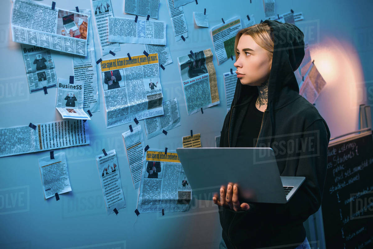 Female hacker with laptop standing in front of wall with newspaper ...