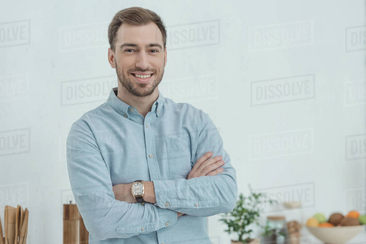 Portrait of smiling man with arms crossed looking at camera at home ...