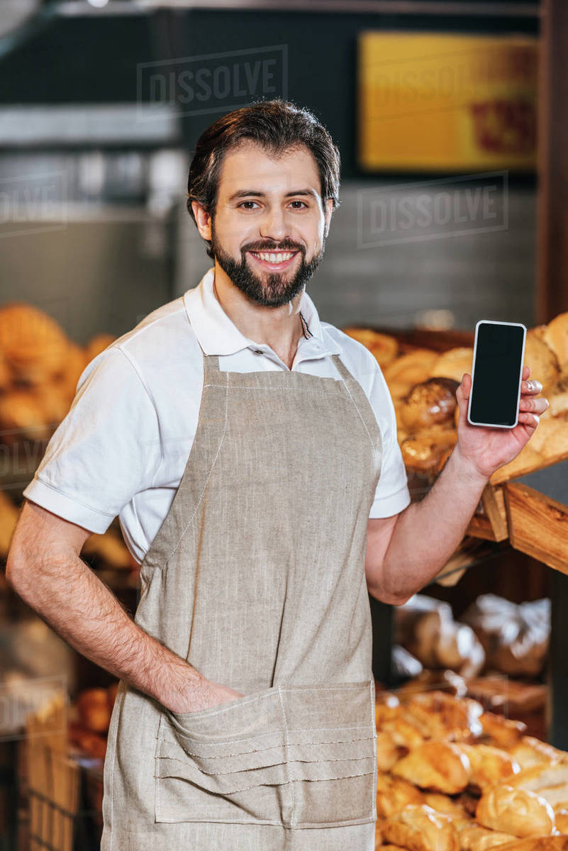 Portrait of smiling shop assistant showing smartphone with blank screen ...