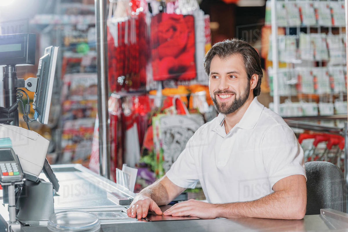 Portrait of smiling male shop assistant at cash point in supermarket ...
