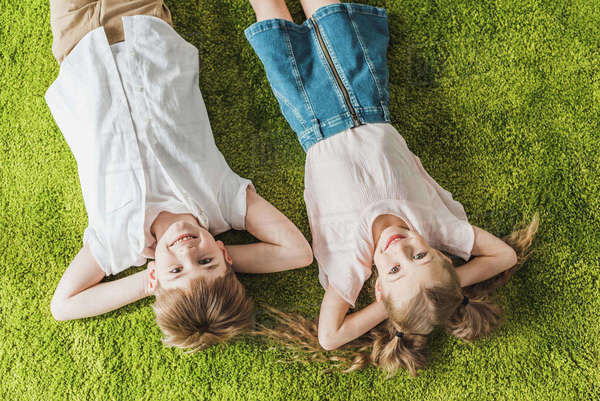 Top view of happy children lying on lawn and smiling at camera ...