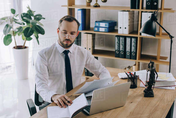 Portrait of lawyer with documents sitting at workplace with laptop in ...