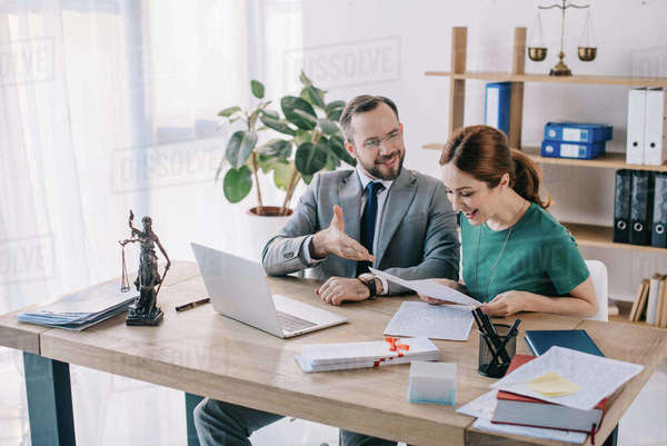 Lawyer and smiling client discussing contract at workplace with laptop ...