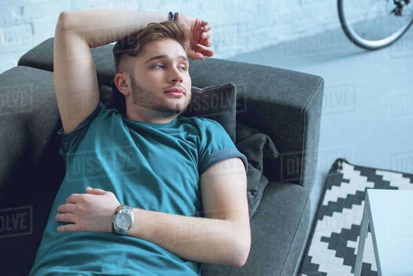 Handsome young man lying on couch and looking away at home - Royalty ...