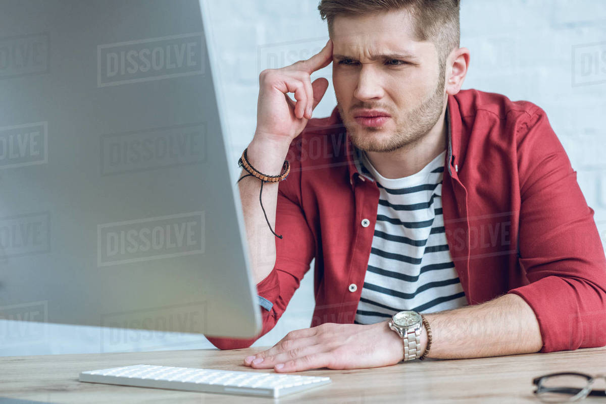 Confused man looking at computer screen - Stock Photo - Dissolve