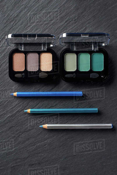 Eye shadows palettes and blue eye pencils on dark slate background ...
