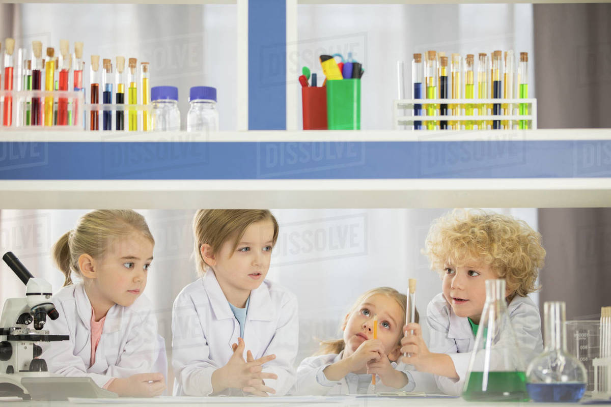 Schoolchildren in lab coats studying together in chemical laboratory ...