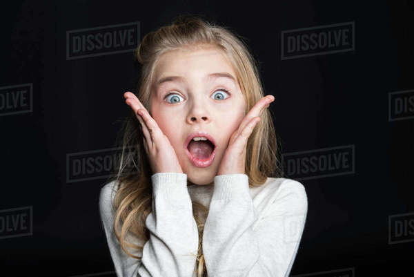 Cute shocked blonde girl looking at camera isolated on black - Royalty ...