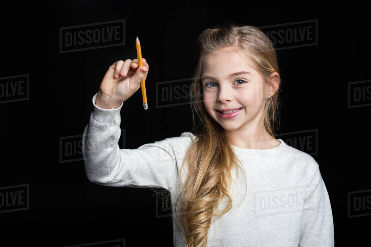 Cute blonde girl holding pencil and smiling at camera isolated on black ...