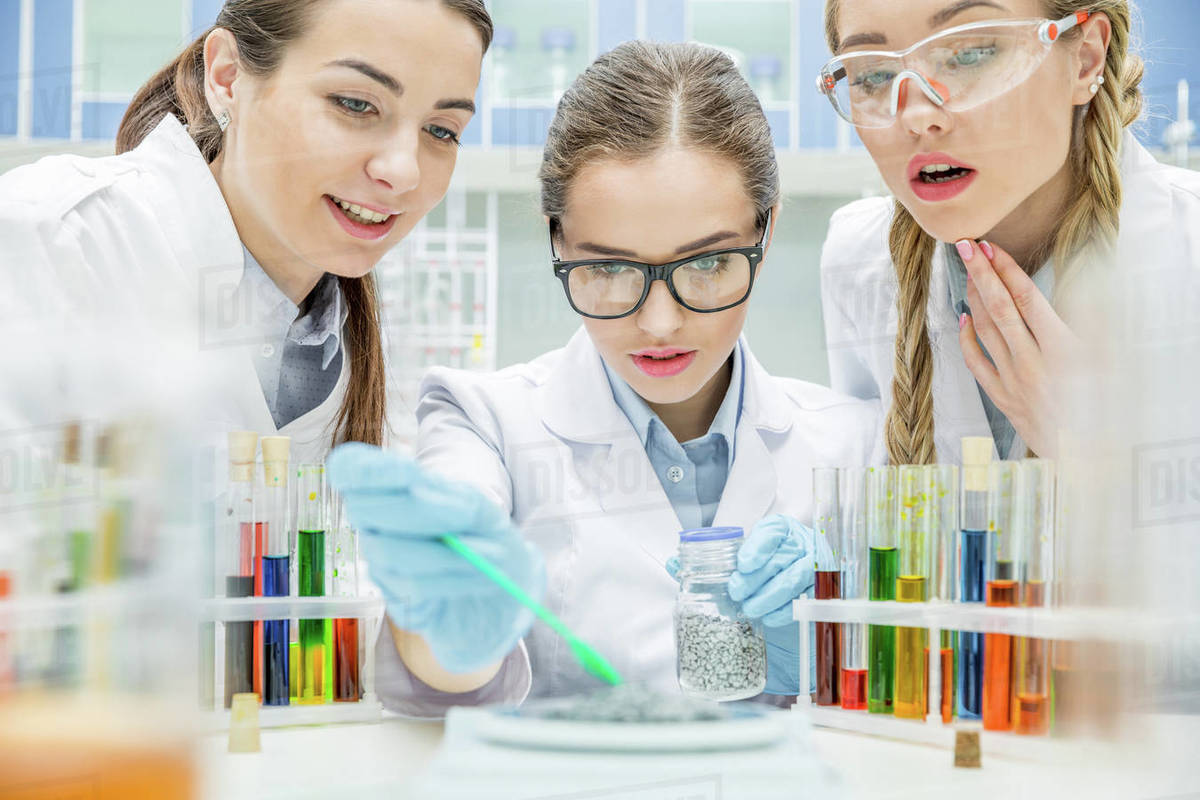 Three young female scientists making experiment in chemical laboratory ...