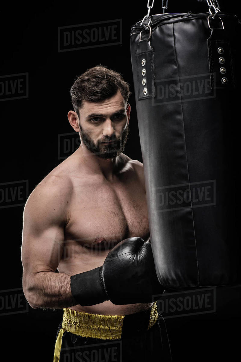 Young muscular boxer standing with punching bag and looking at camera ...