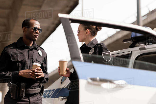 Young relaxing police officers drinking coffee near police car ...