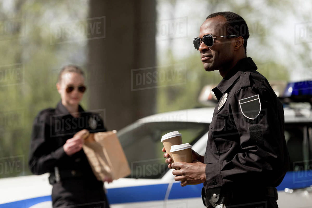 Young police officers with coffee to go and paper bag with lunch having ...
