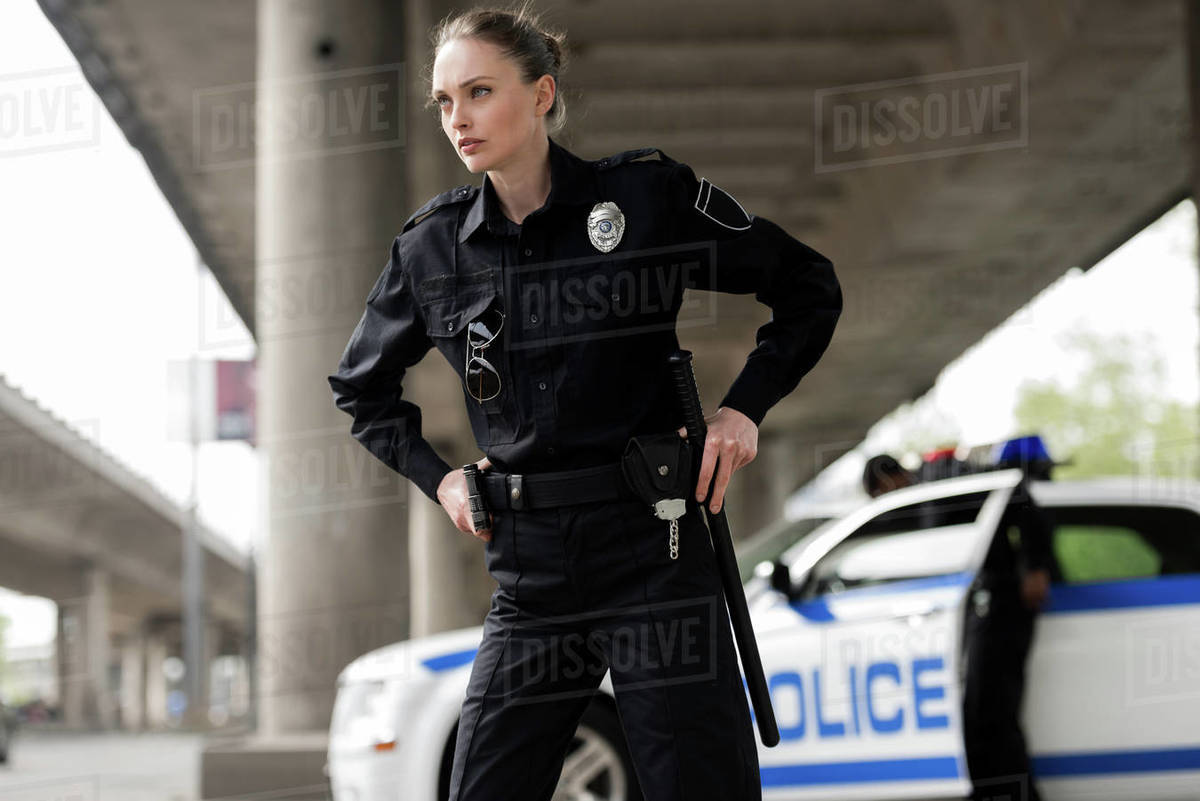 Confident female police officer looking away and taking out gun and bat ...