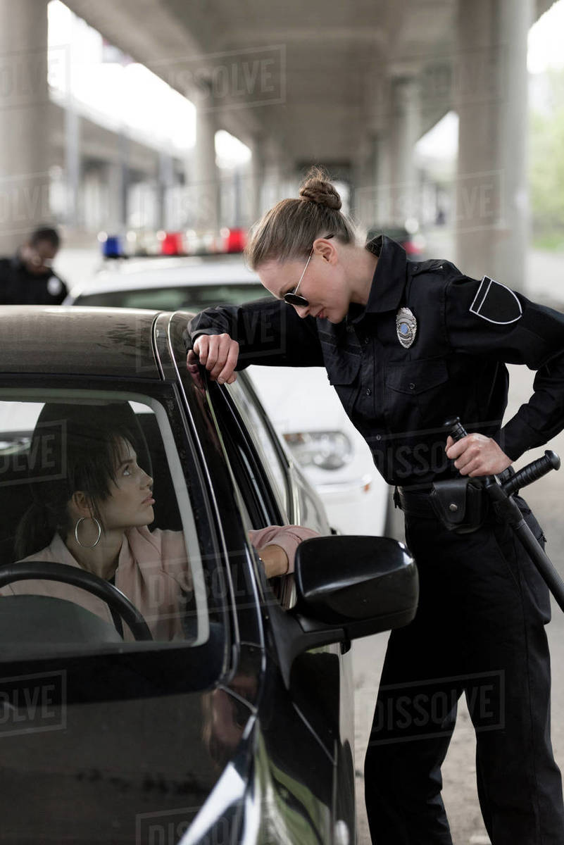 Side view of policewoman holding truncheon and talking to young woman ...