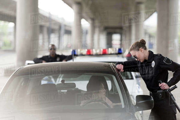 Policewoman in sunglasses talking to woman sitting in car and policeman ...