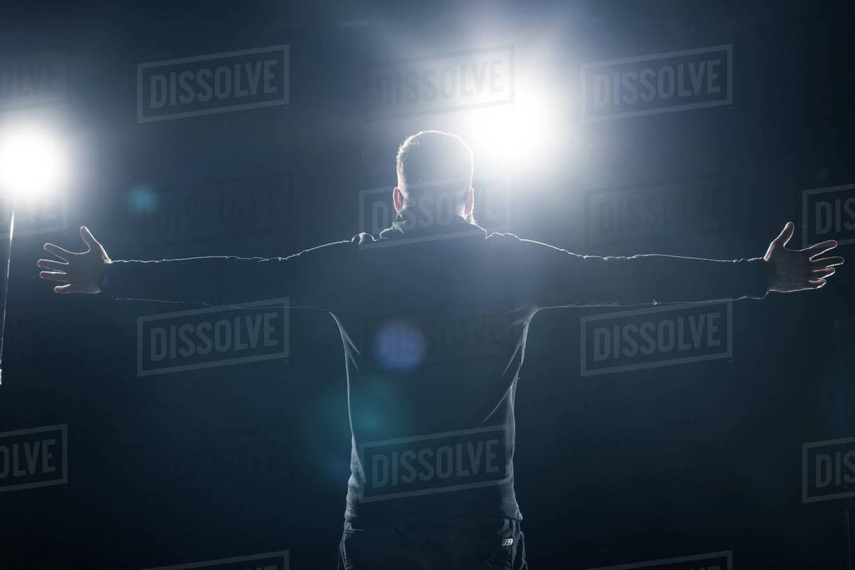 Man in black clothes standing with outstretched arms in bright light ...