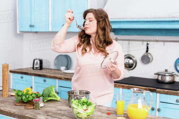 Portrait of young overweight woman cooking soup in kitchen at home ...