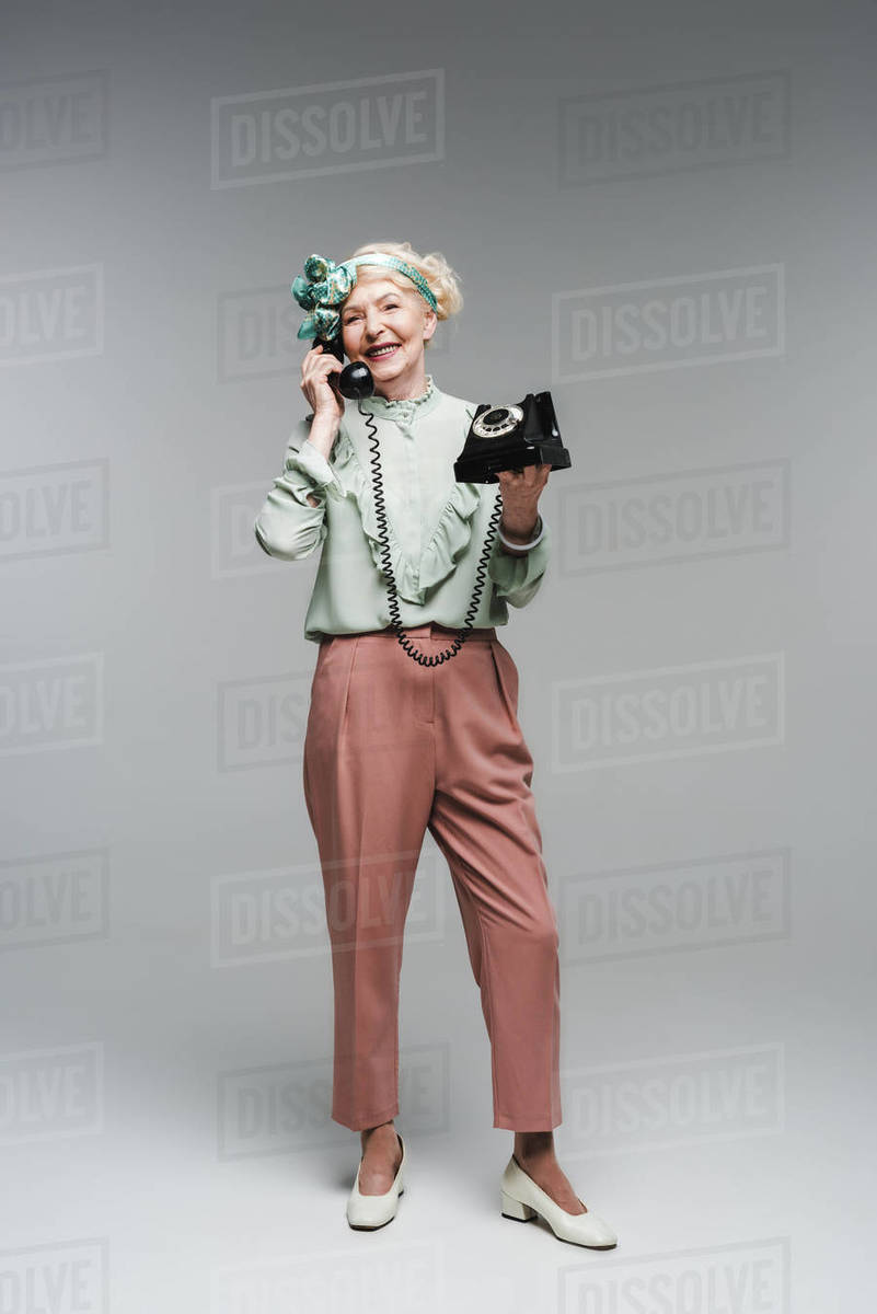Happy senior woman talking by rotary phone on grey - Stock Photo - Dissolve