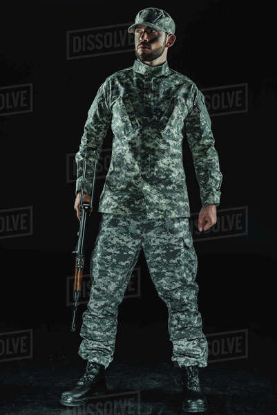 soldier in military uniform with rifle looking away isolated on black ...