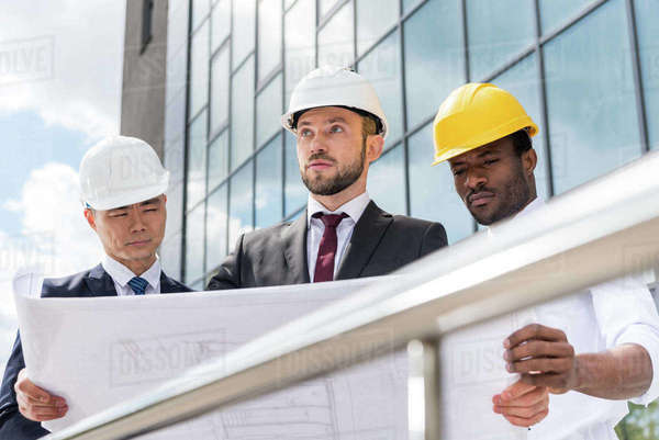 Multiethnic group of professional architects in helmets working with ...